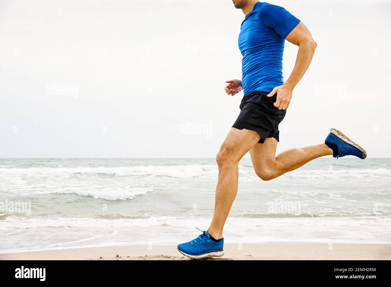 closeup male runner running sandy beach in background of sea and sky ...