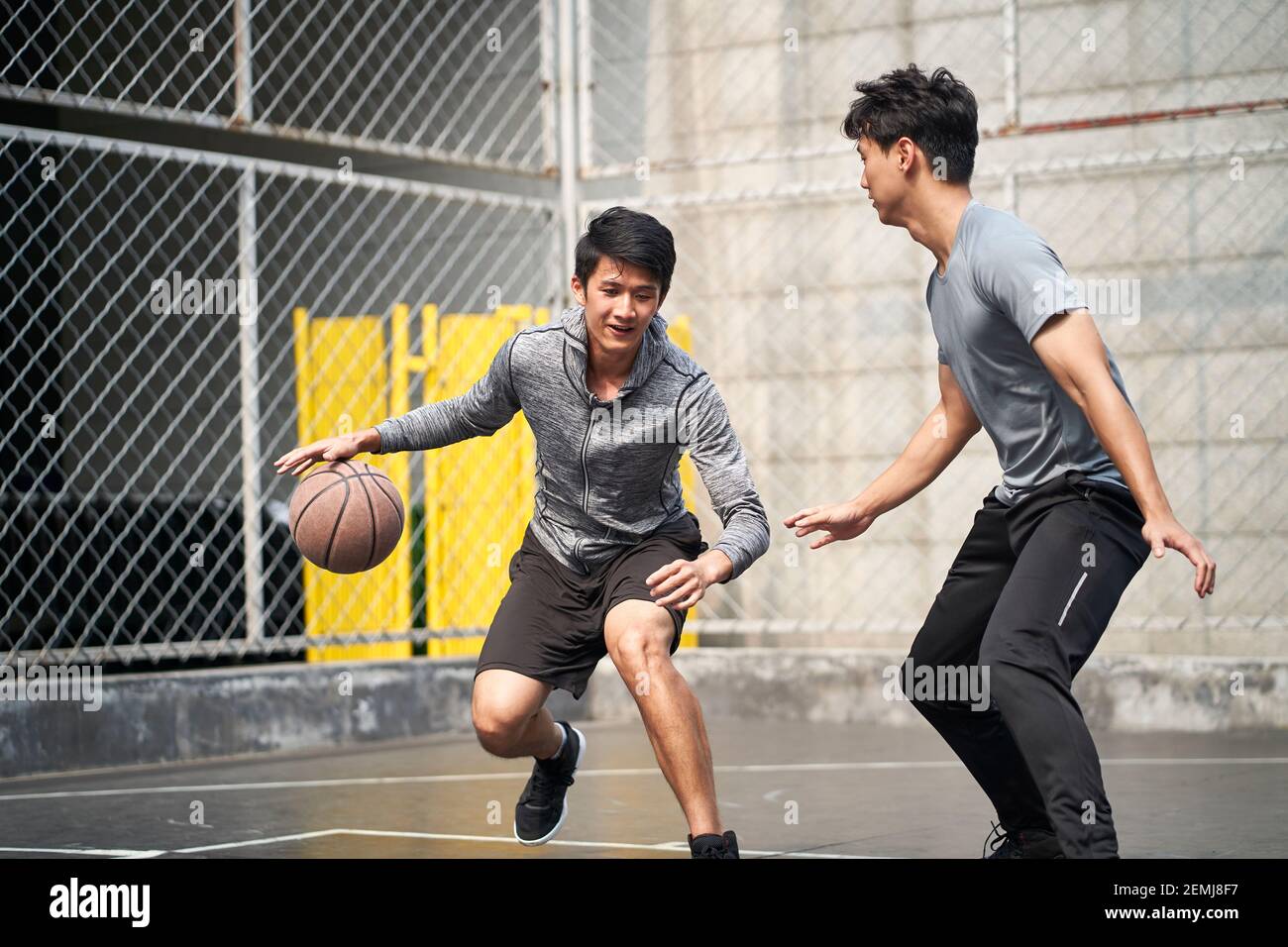 two young asian adult men playing one-on-one basketball on outdoor ...