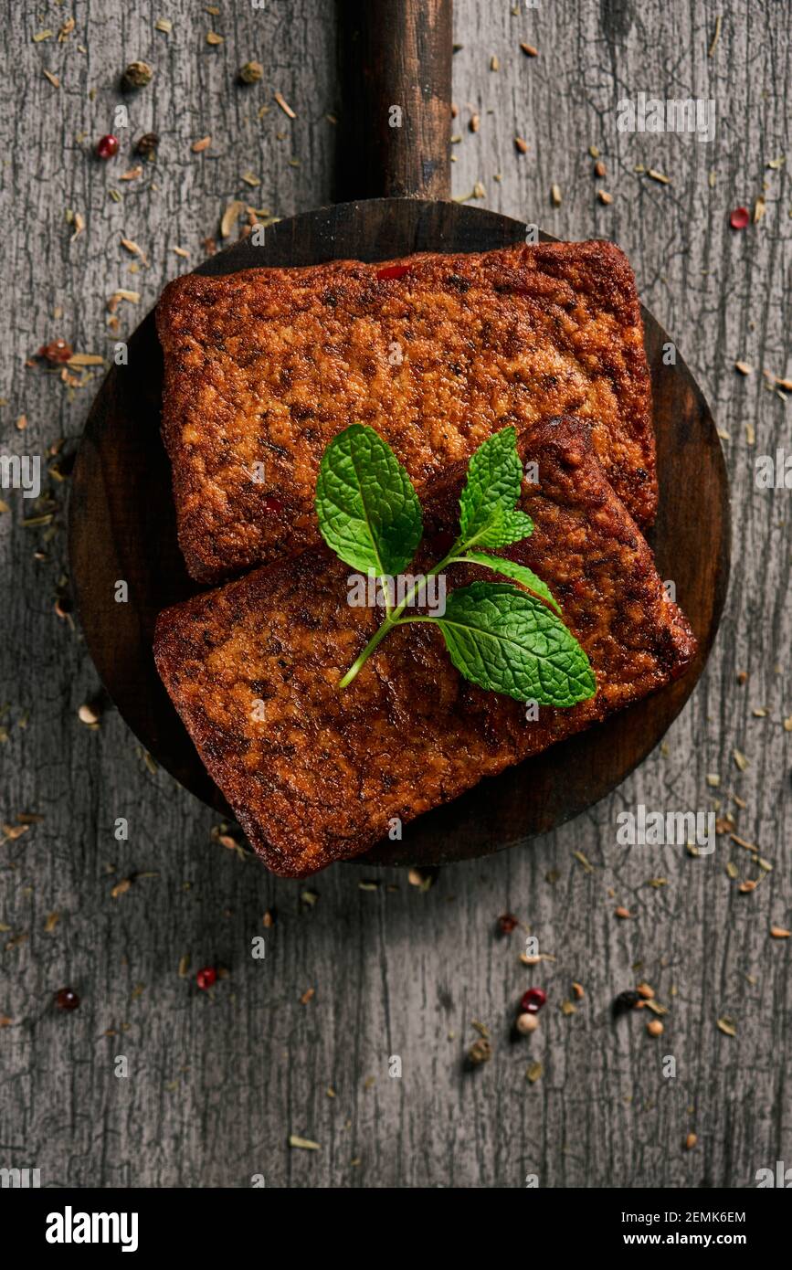 high angle view of some cooked tofu fillets in a round dark wooden tray ...
