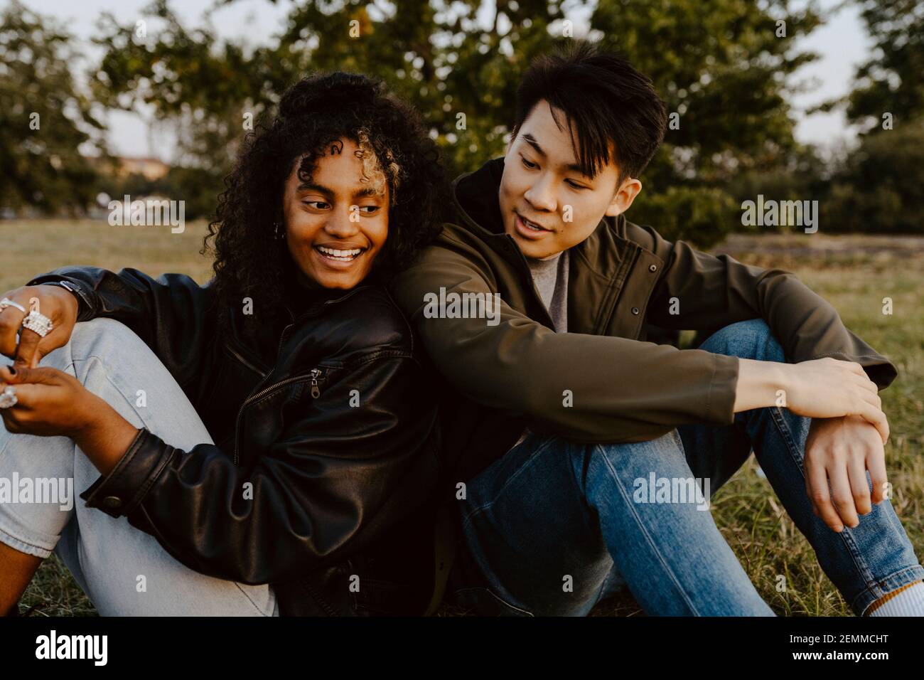 Happy friends sitting side by side in park during sunset Stock Photo ...