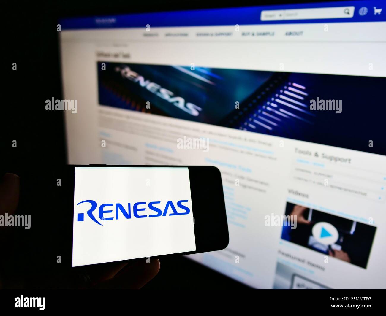 Person holding mobile phone with logo of semiconductor company Renesas ...