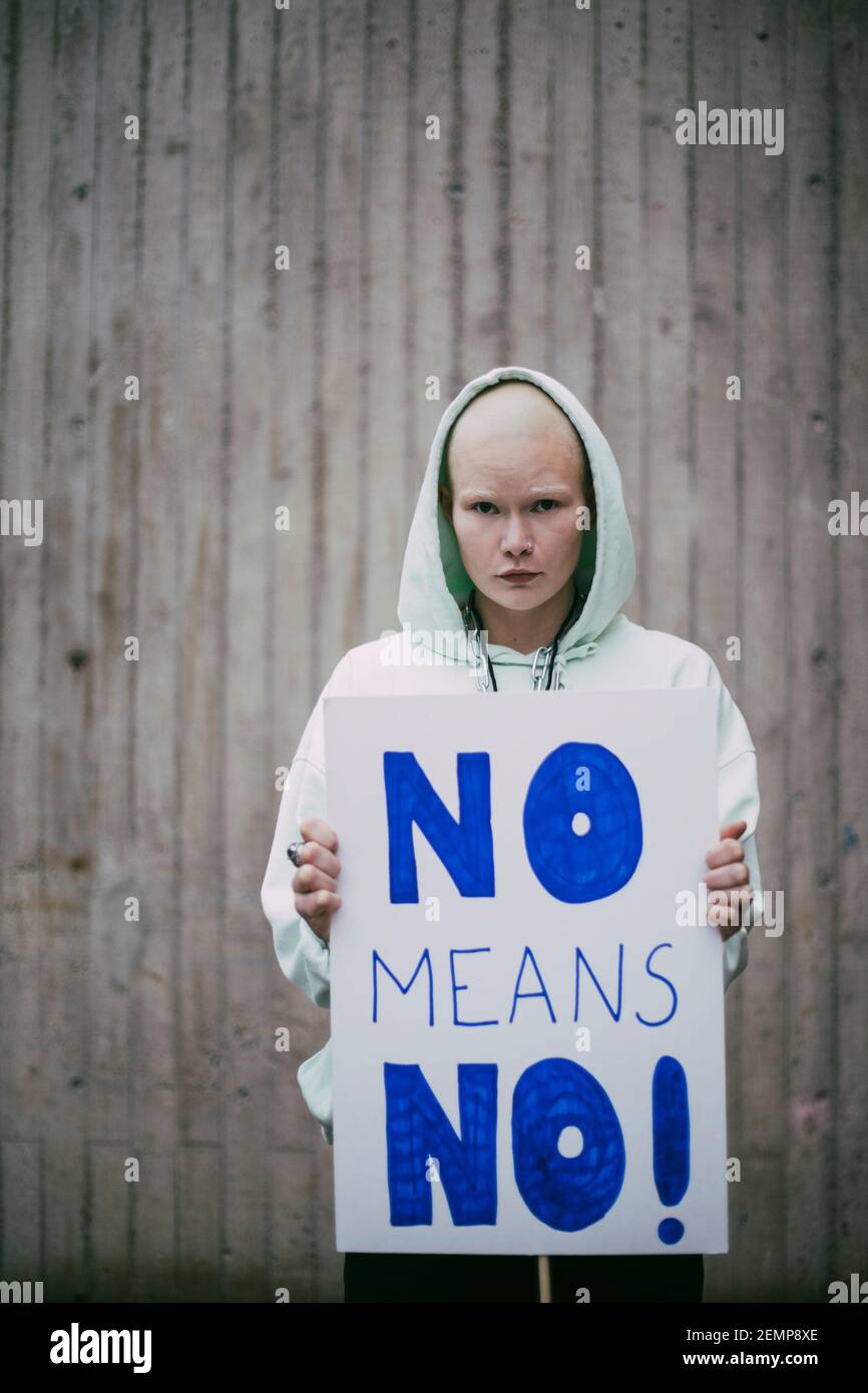 Portrait of female activist holding no means no poster against wall ...