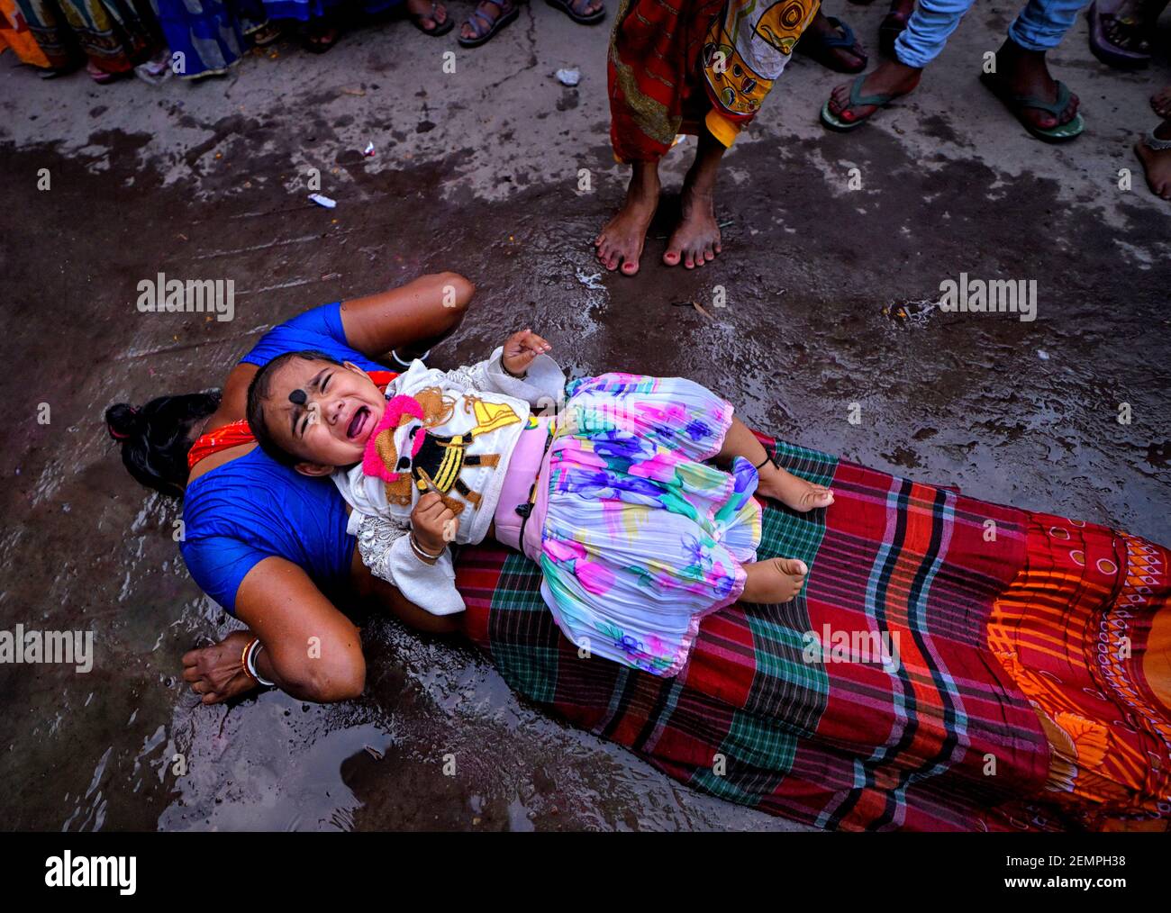 A hindu woman seen lying on the ground with a kid on her back as a ...