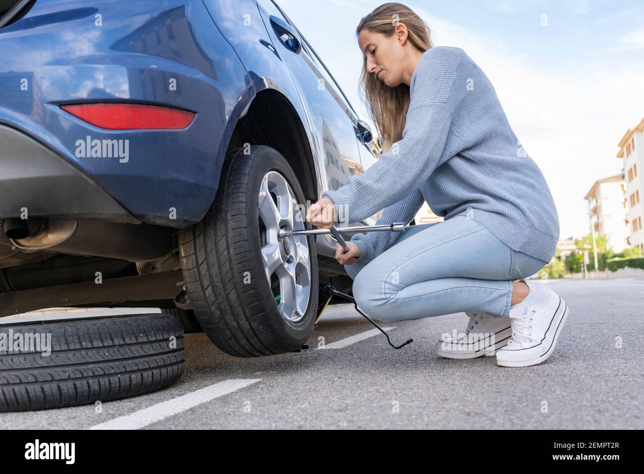 Young beautiful female using force trying to unscrew the wheel bolts ...