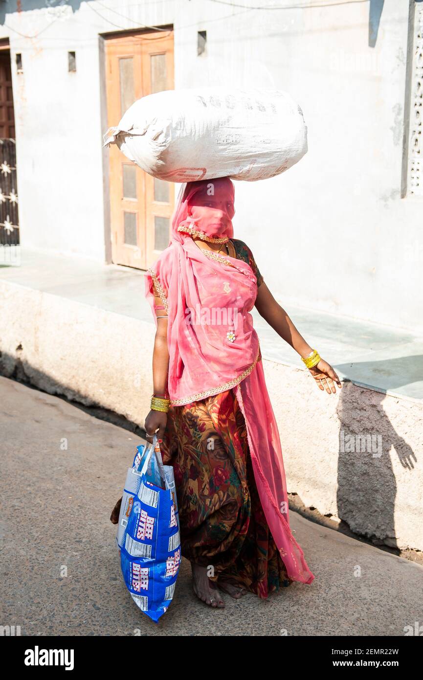 An Indian woman walks with a large bag on her head, through the streets ...