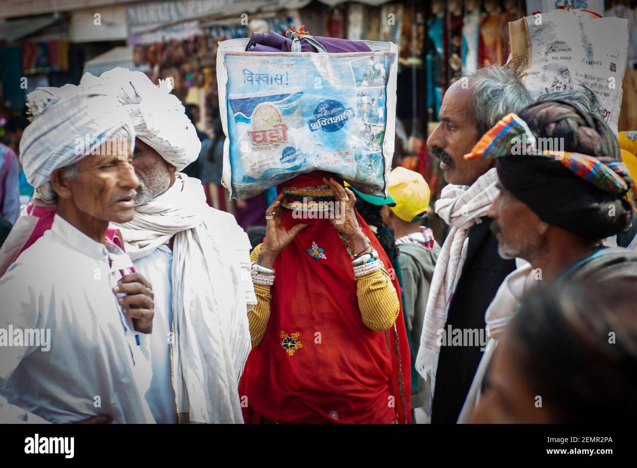 An indian woman carrying a bag on her head, and covering her face with ...