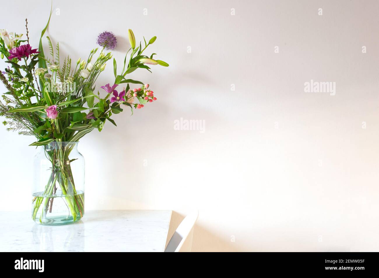 Beautiful spring flowers in glass vase on white table near white wall ...