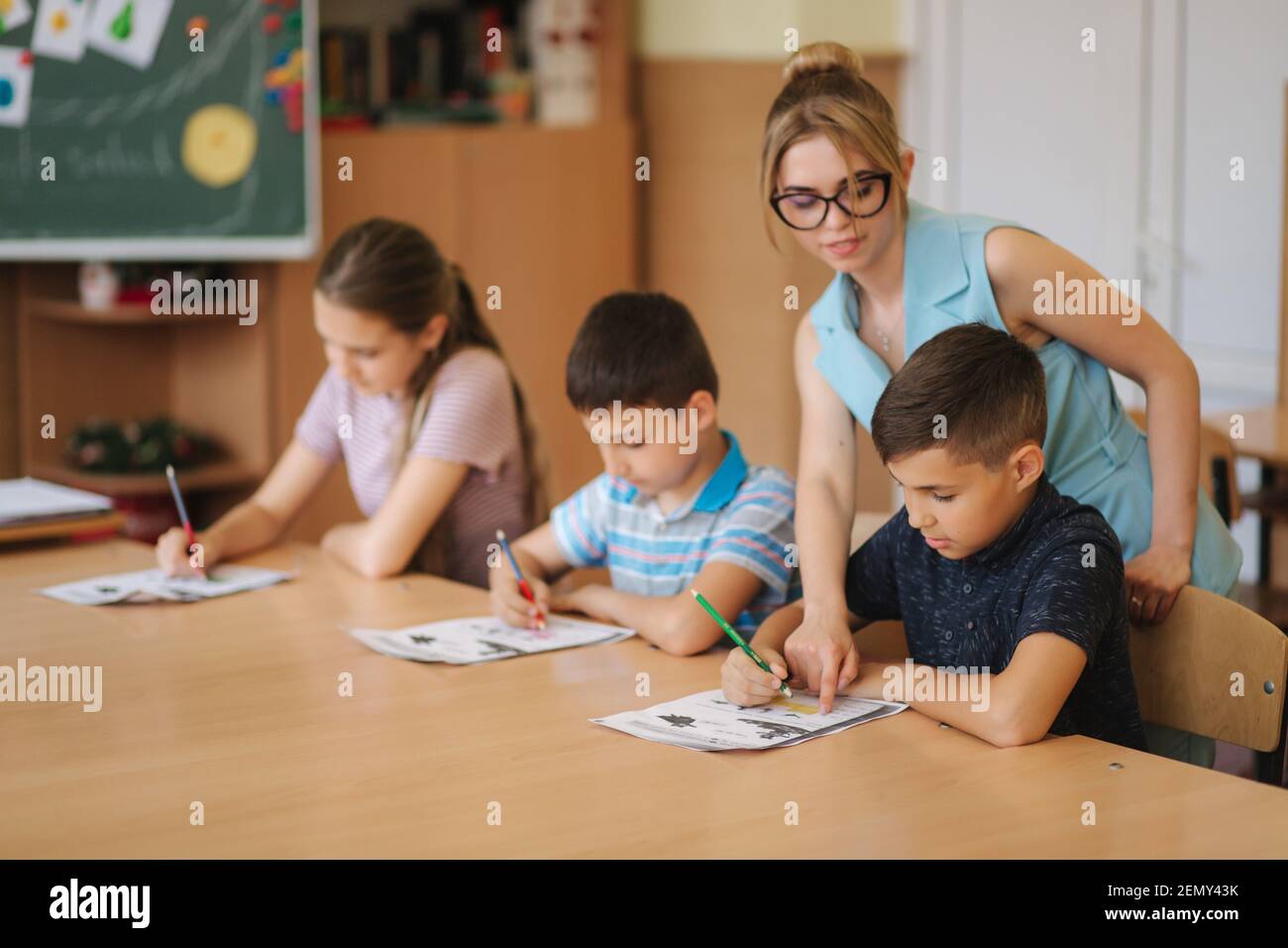 Teacher helping school kids writing test in classroom. education ...