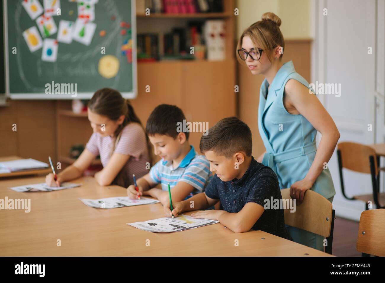 Teacher helping school kids writing test in classroom. education ...