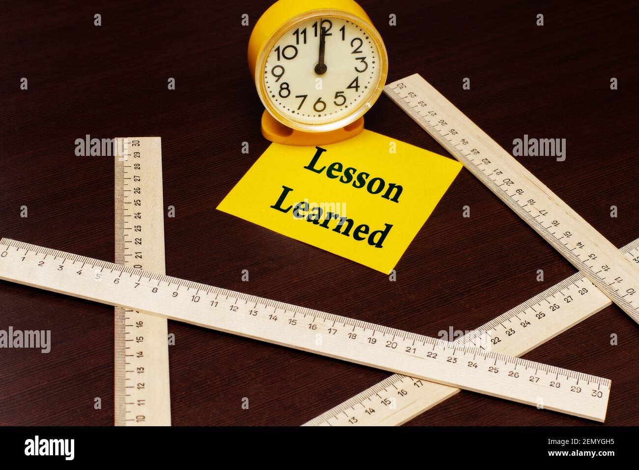 Message LESSON LEARNED on a yellow sticky note next to a yellow clock ...