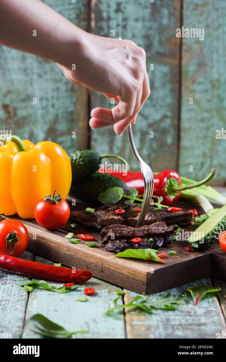 Woman hand with fork picking steak on oak board served with raw ...
