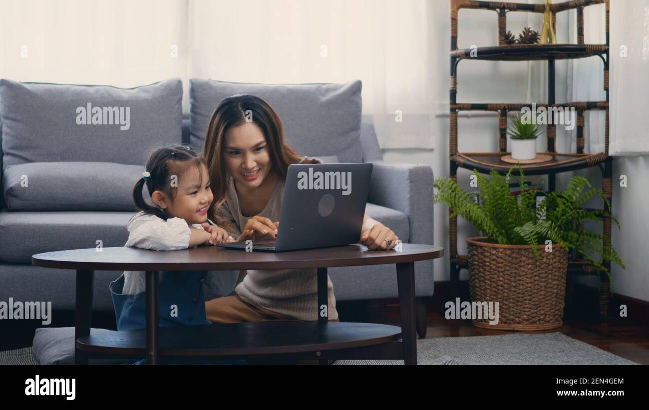 Asian young mother with laptop computer teaching her kid to learn or ...