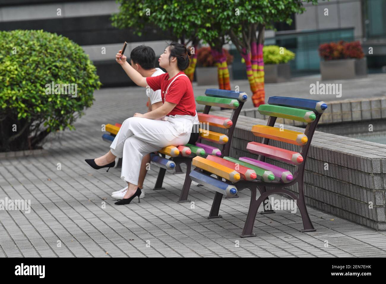A young Chinese couple sits on a colored pencil bench next to others at ...