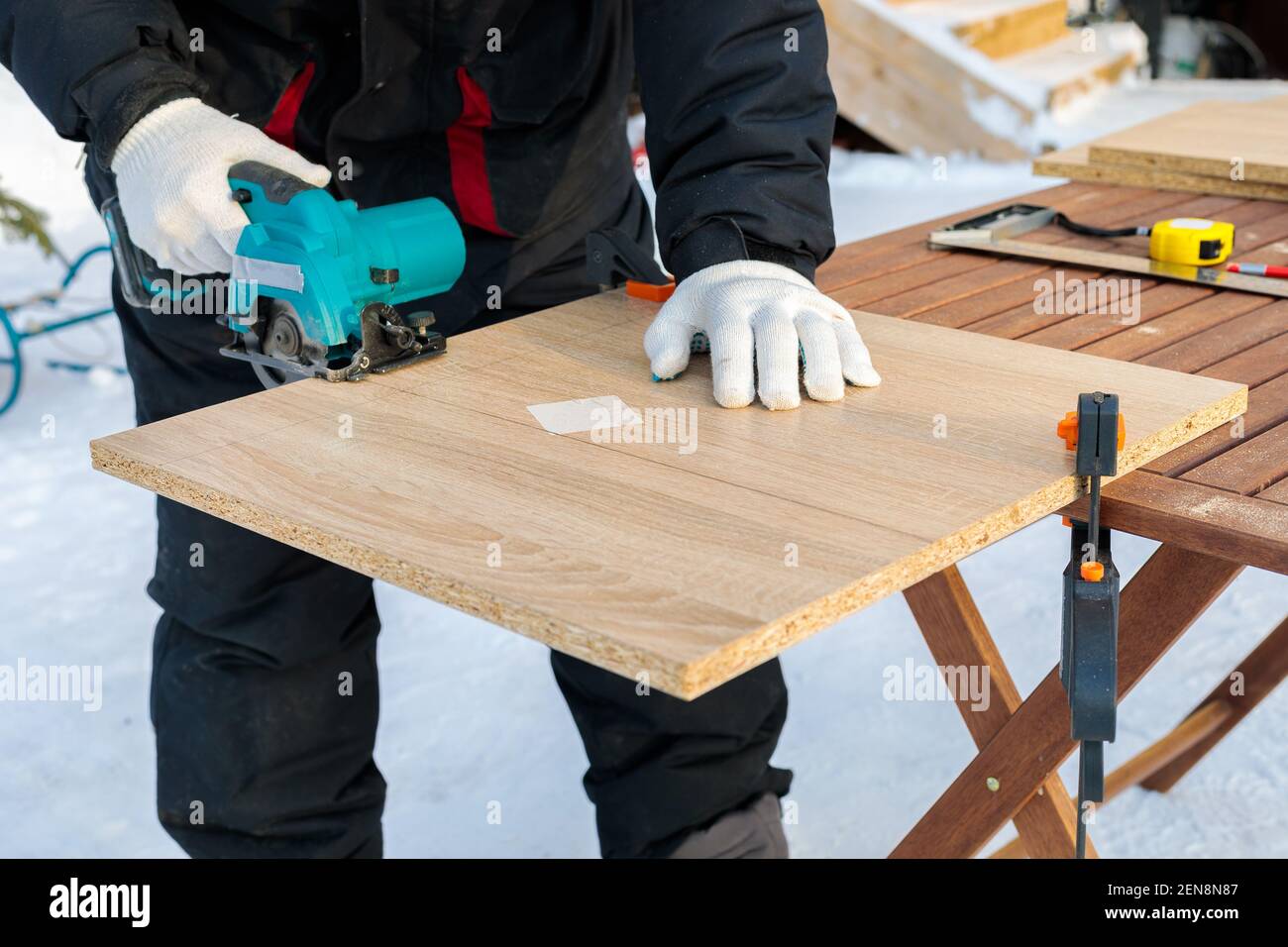 A male worker cuts a wooden panel attached to a workbench with clamps ...