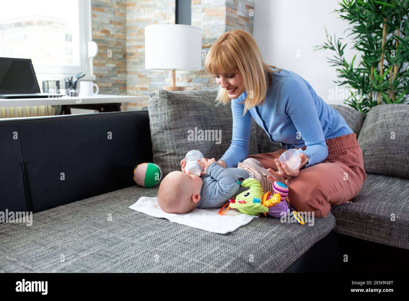 Loving mom giving her baby some water as they sit and lay on the couch ...