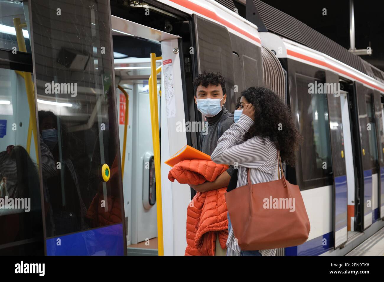 Young latin couple wearing protective face mask going inside the train ...