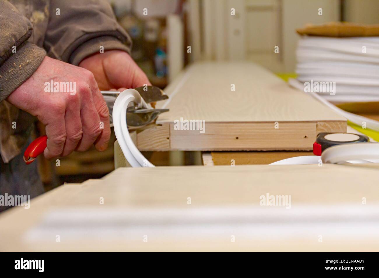Carpentry worker is holding red metal pliers and cutting rubber tape ...