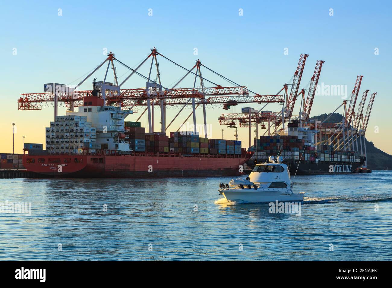 Two large container ships taking on cargo while a pleasure boat passes ...