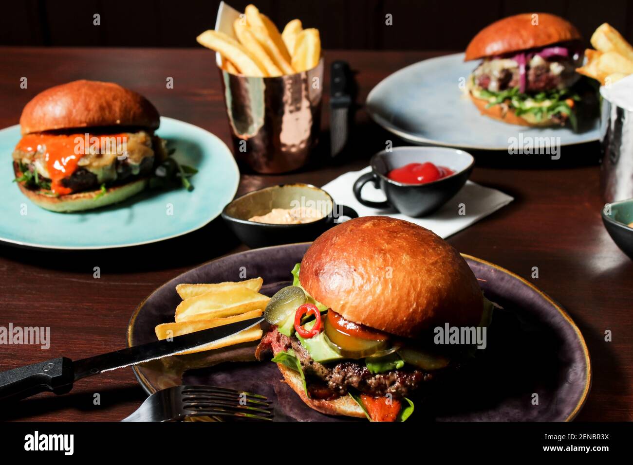 Different burgers on the table, served frenc fries and sauces on plates ...