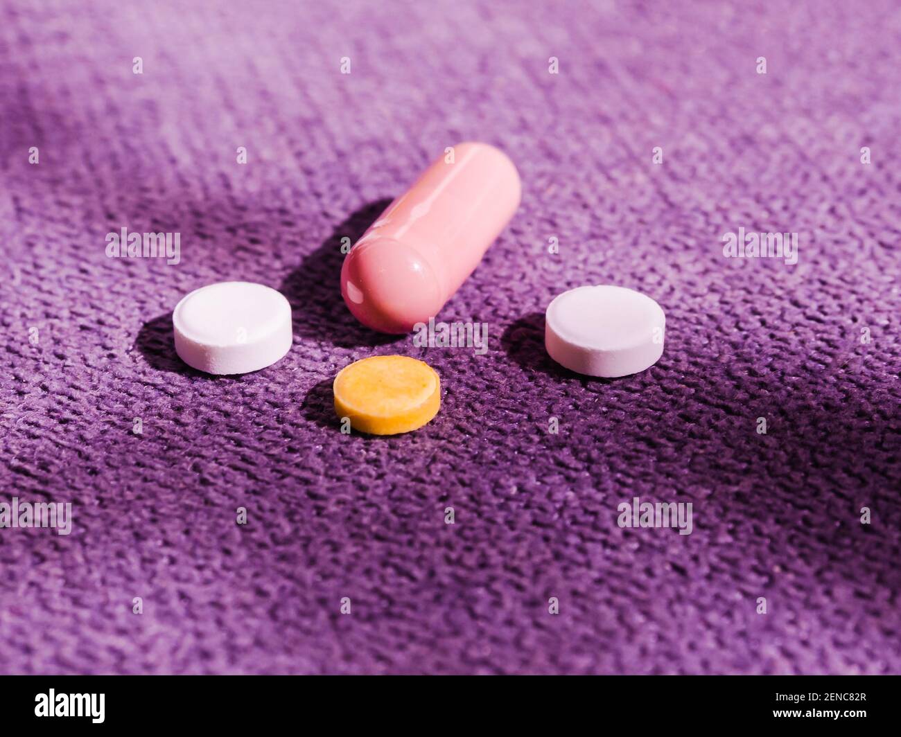 A pink capsule and three round tablets lie on violet vilvet surface ...