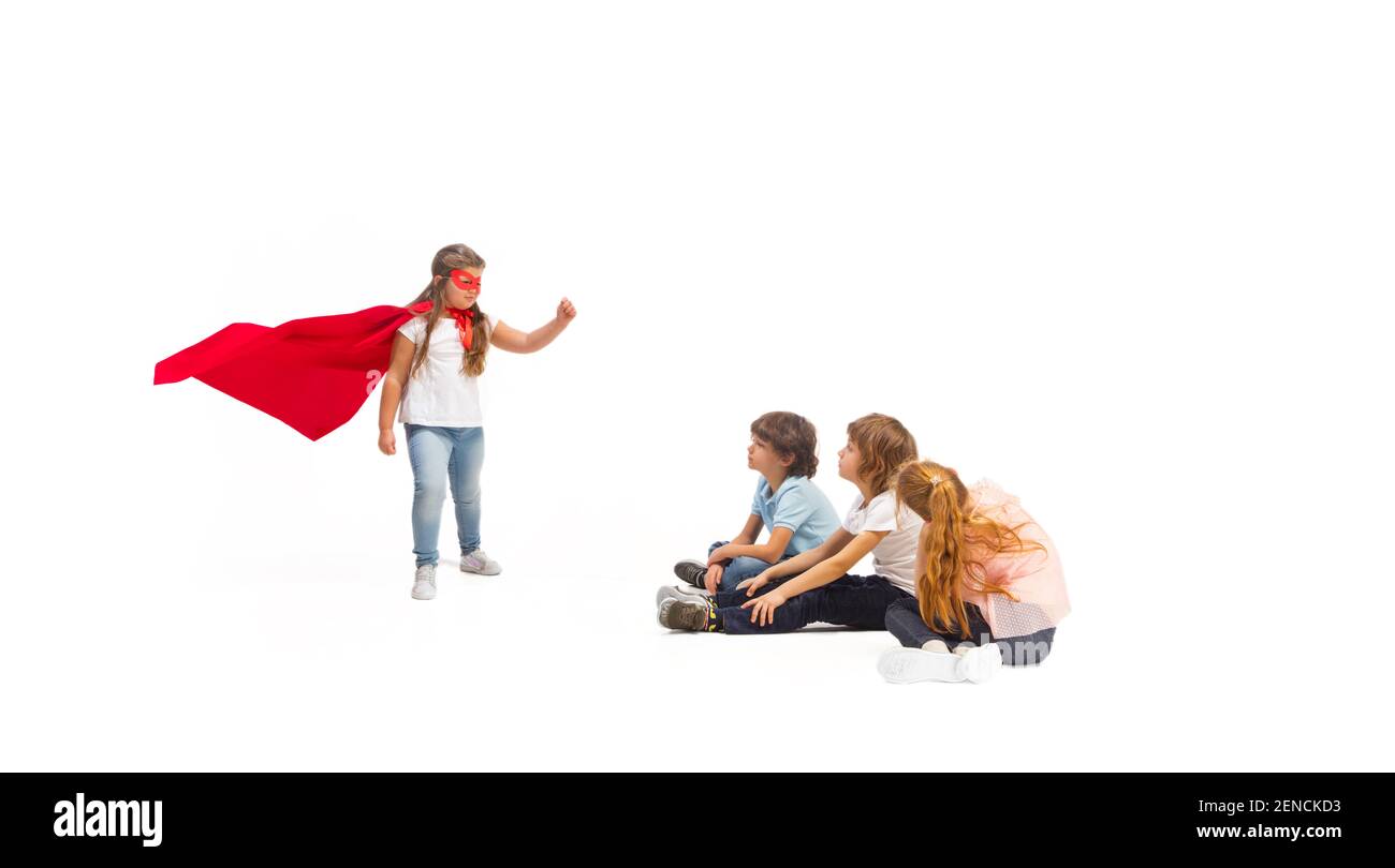 Cool. Child pretending to be a superhero with her friends sitting ...