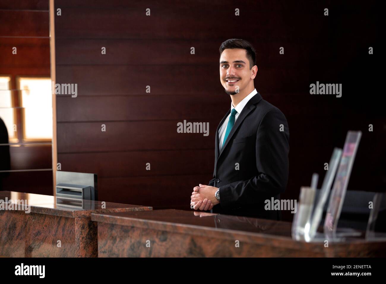 Young receptionist standing behind the front desk ready to welcome ...