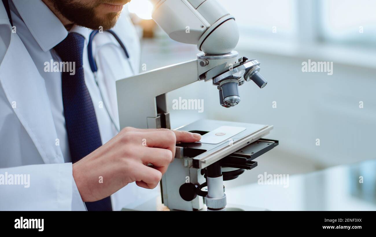 scientist looking through a microscope sitting at a laboratory table ...