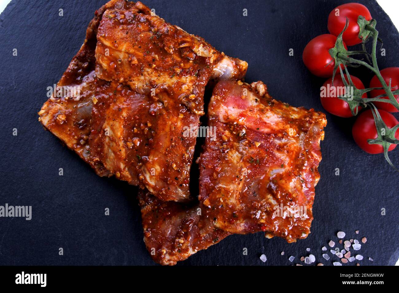 Raw marinated pork ribs on black stone plate ready for cooking. Raw bbq ...