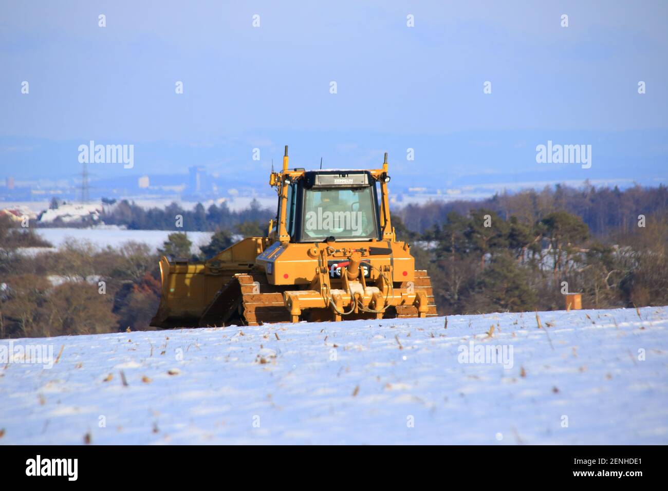 Caterpillar drives over a field in winter and spreads earth Stock Photo ...
