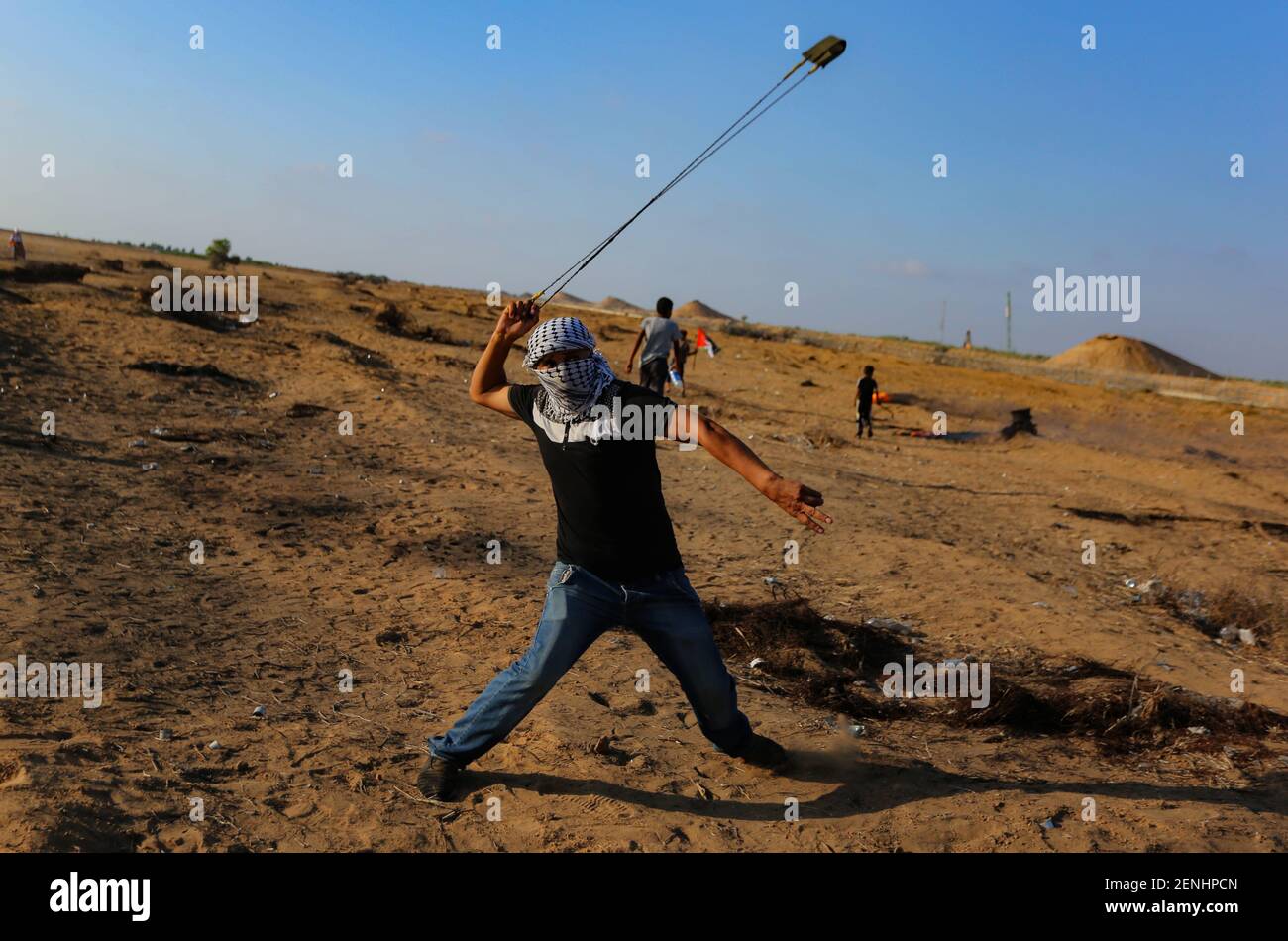 A Palestinian demonstrator throws stones using a slingshot during an ...