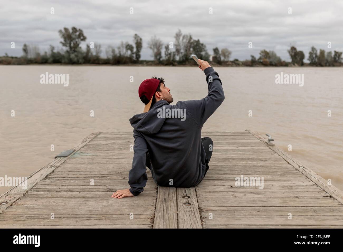 Young man from behind wearing a red cap and a grey sweater is sitting ...
