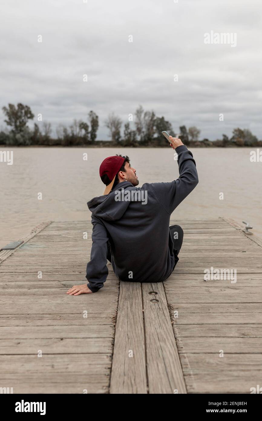 Young man from behind wearing a red cap and a grey sweater is sitting ...