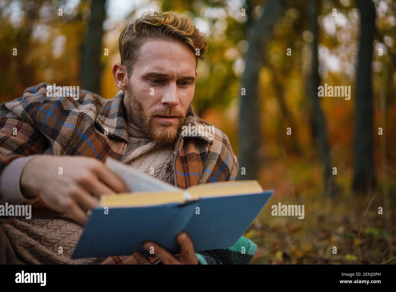 Handsome unshaven man reading book while resting in autumn forest Stock ...