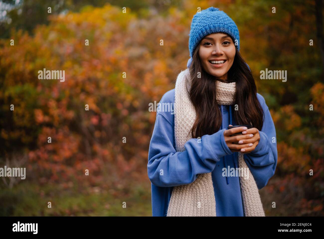 Nice brunette happy woman in knit hat drinking tea while strolling in autumn forest Stock Photo ...