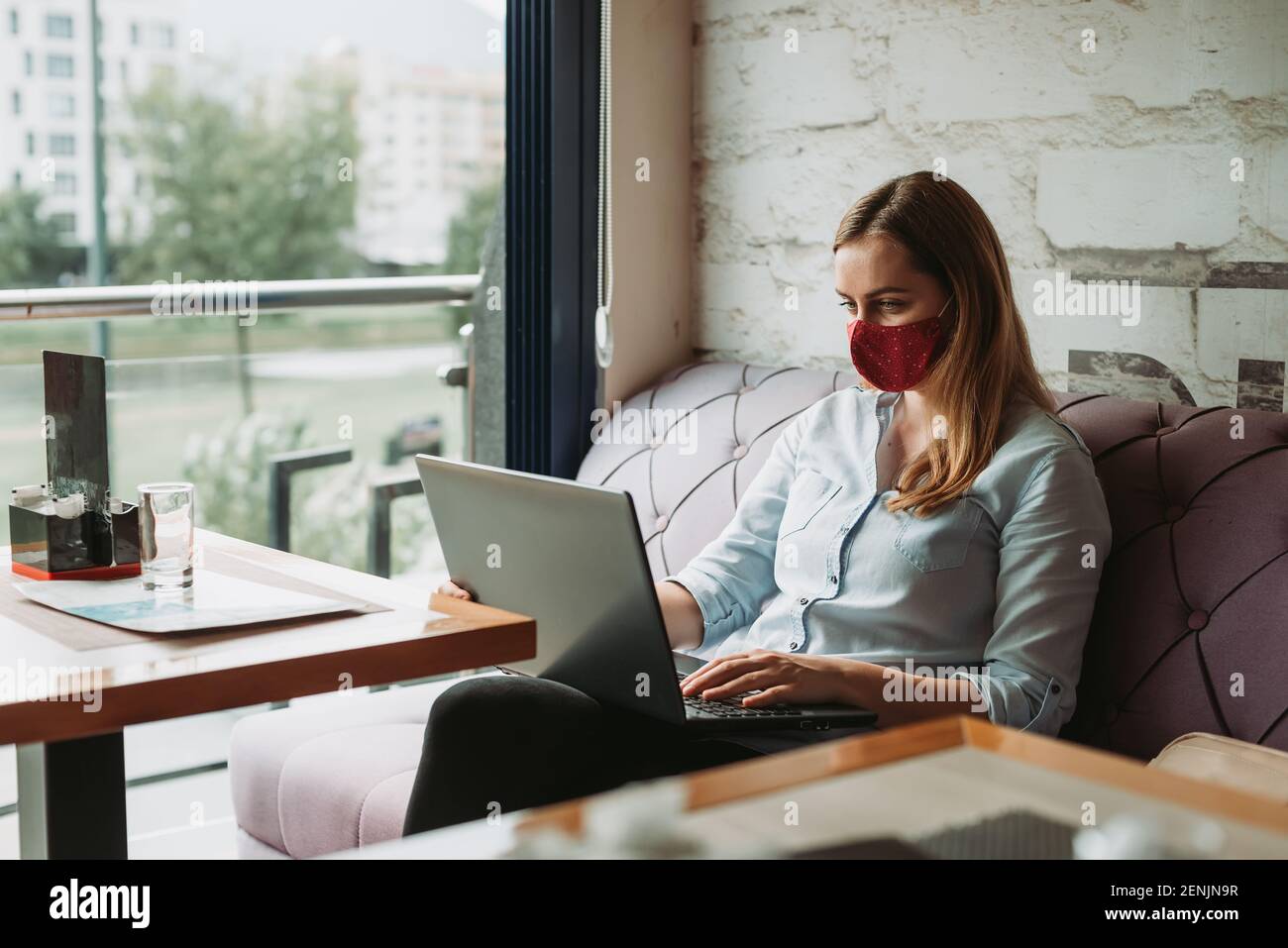 Woman freelancer indoors with face mask working on laptop in coffee ...