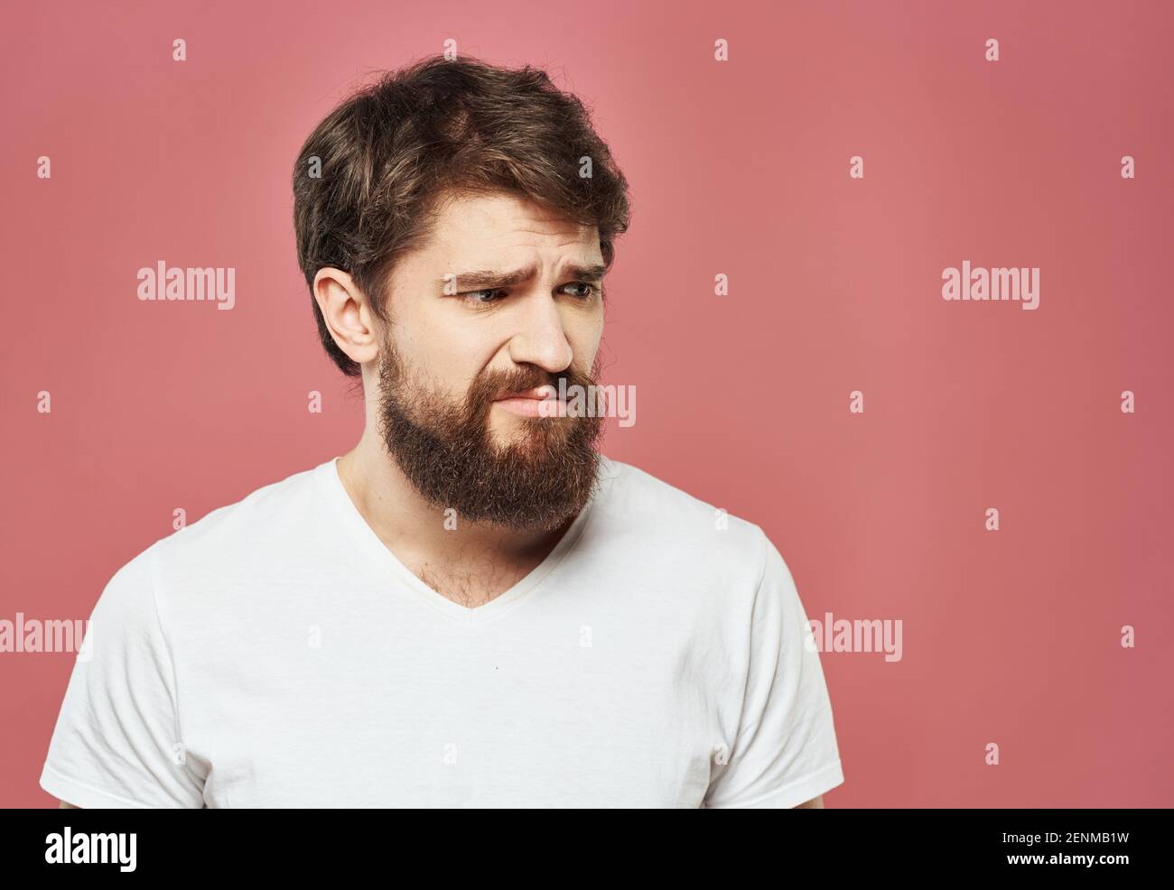 Portrait of an upset man in a white t-shirt on a pink background ...