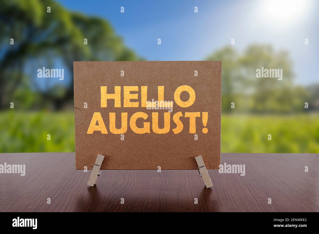 Hello August text on card on the table with sunny green park background ...