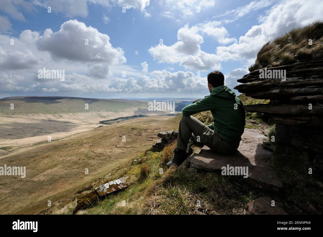 A caucasian male walker sitting on a ledge overlooking the valley ...