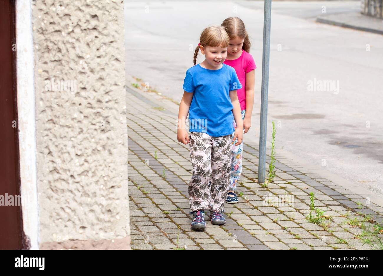 Two happy little girls, school age children walking on the sidewalk ...