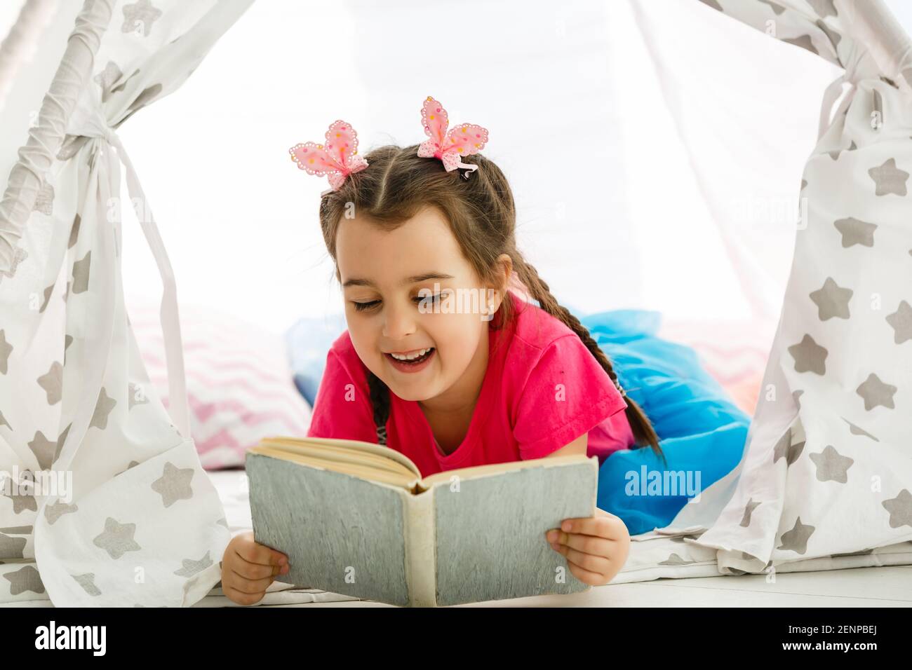 Portrait of pretty little girl reading book in cozy living room at home ...