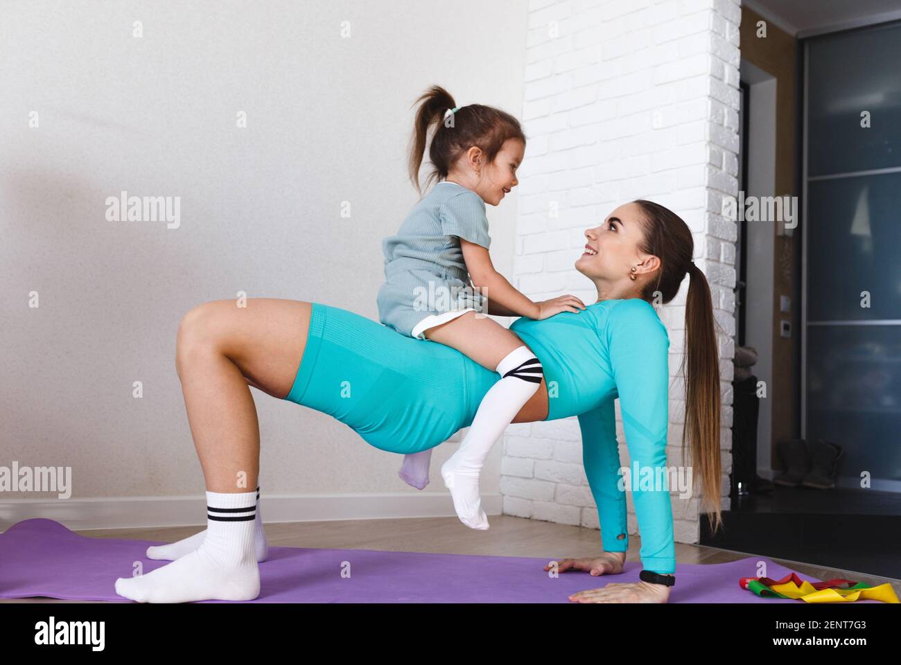 A young athletic mother and a girl do exercises together at home ...