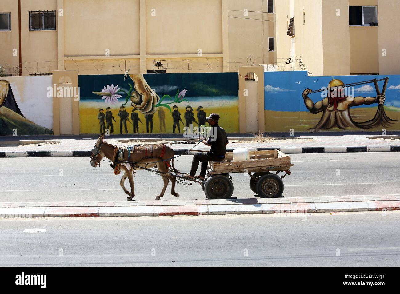 Palestinians ride a donkey cart walks next to past a mural along a ...
