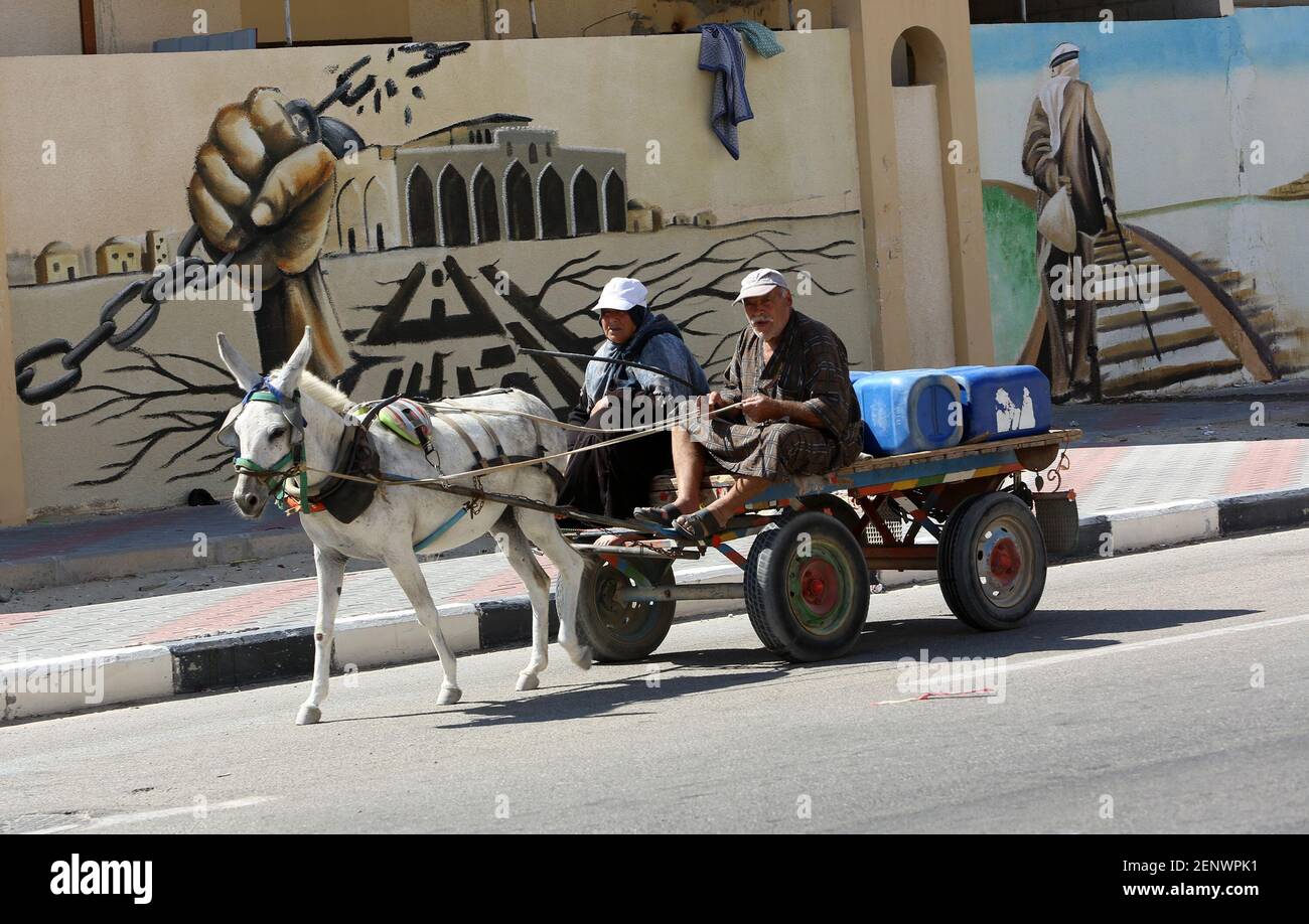 Palestinians ride a donkey cart walks next to past a mural along a ...