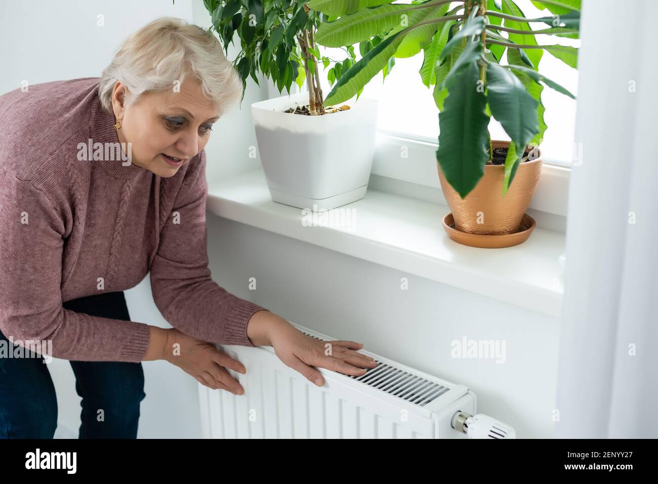 Senior woman trying to keep warm by warming hands on the heating ...