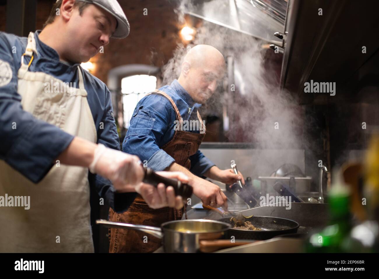 Adult men adding spices and frying dish while working together in cafe ...