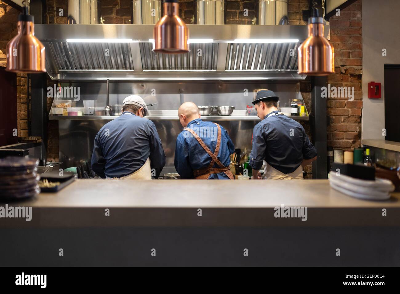 Anonymous male cooks preparing food behind counter together during work ...