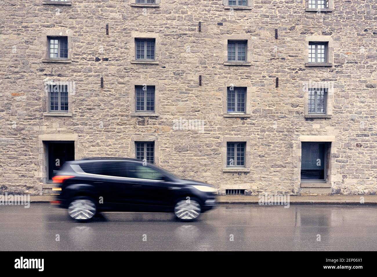 Abstract of car driving along road with stone walled building behind ...