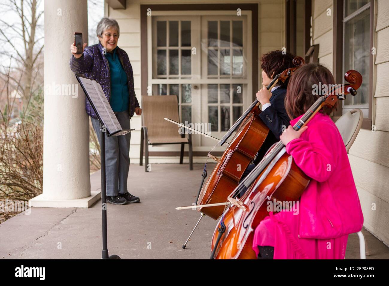 An elderly woman records two children giving cello concert on porch ...