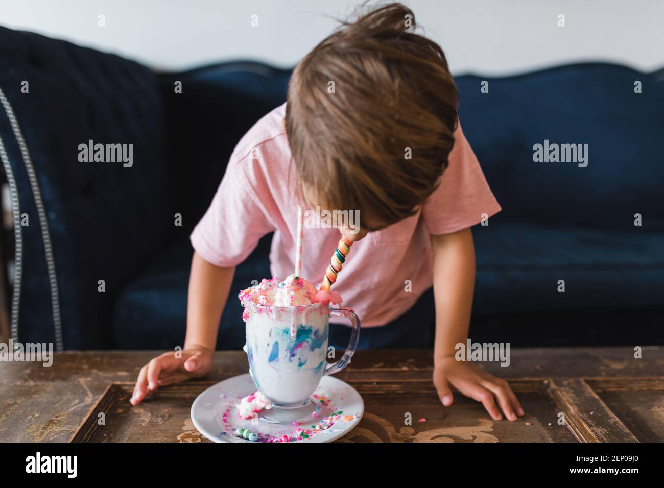 Boy drinking a colorful milk shake in front of a vintage blue couch ...