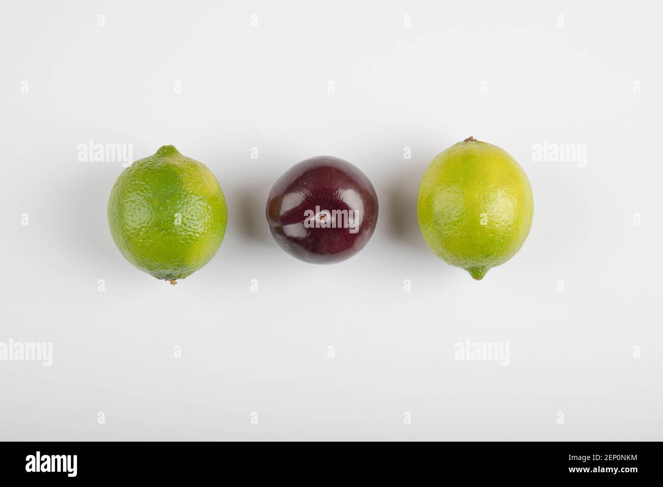 Two lime fruits and one plum on white background Stock Photo - Alamy